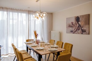 Uma sala de jantar com mesa posta para seis pessoas, cadeiras, um lustre e um quadro na parede.