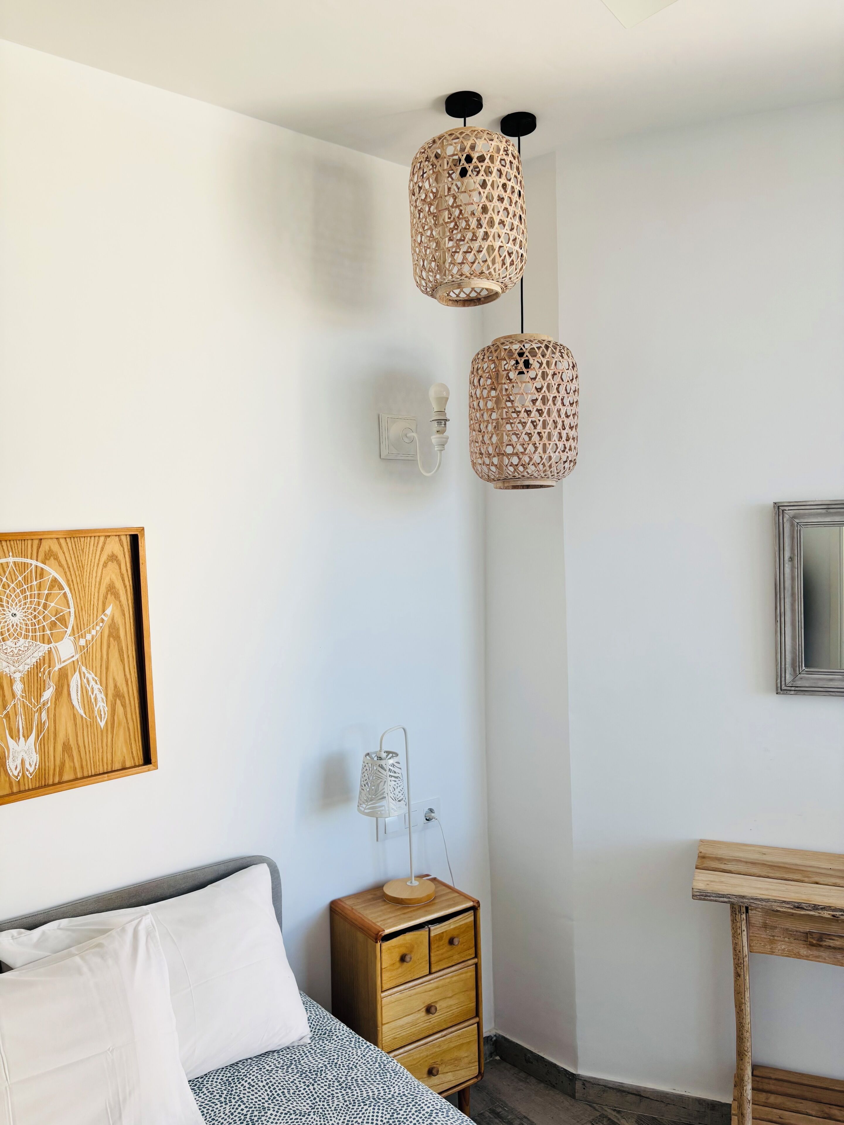 Quarto com cama, mesa de cabeceira, luminária na parede e duas luminárias pendentes.