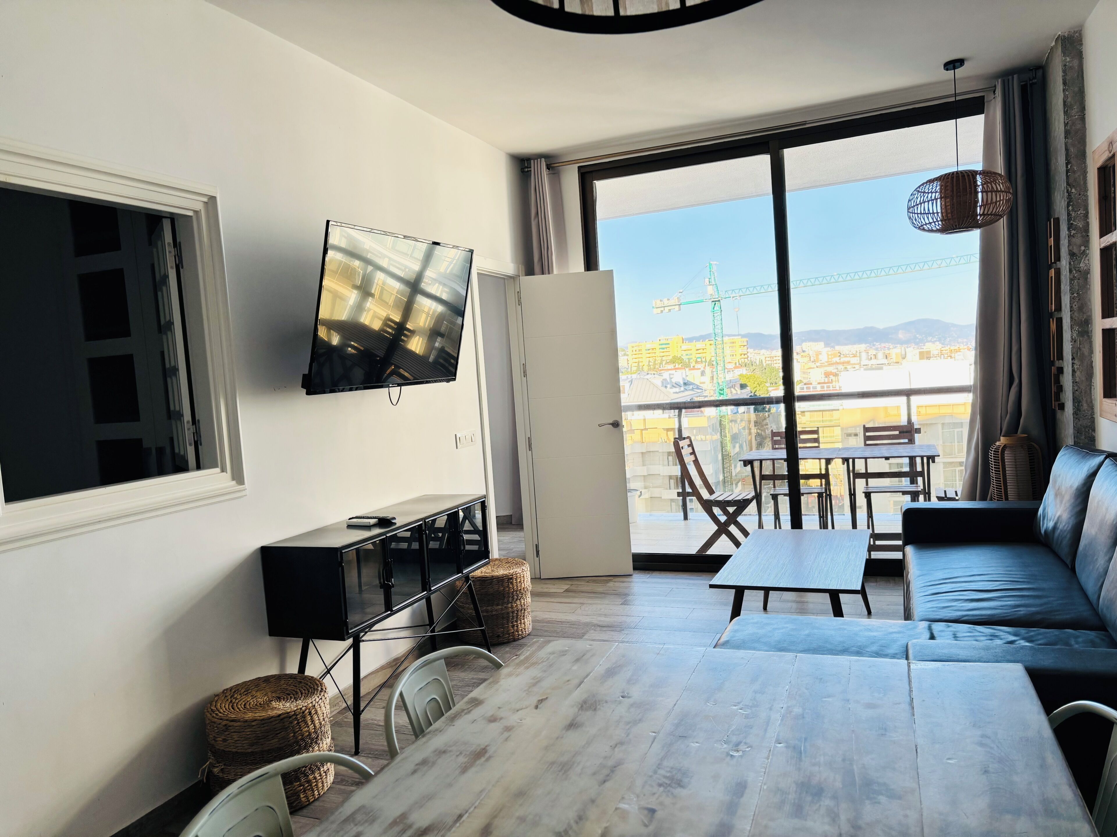 Uma sala de estar moderna com televisão de tela plana, sofá, mesa de jantar com cadeiras e varanda com vista para a cidade.