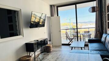 Uma sala de estar moderna com televisão de tela plana, sofá, mesa de jantar com cadeiras e varanda com vista para a cidade.