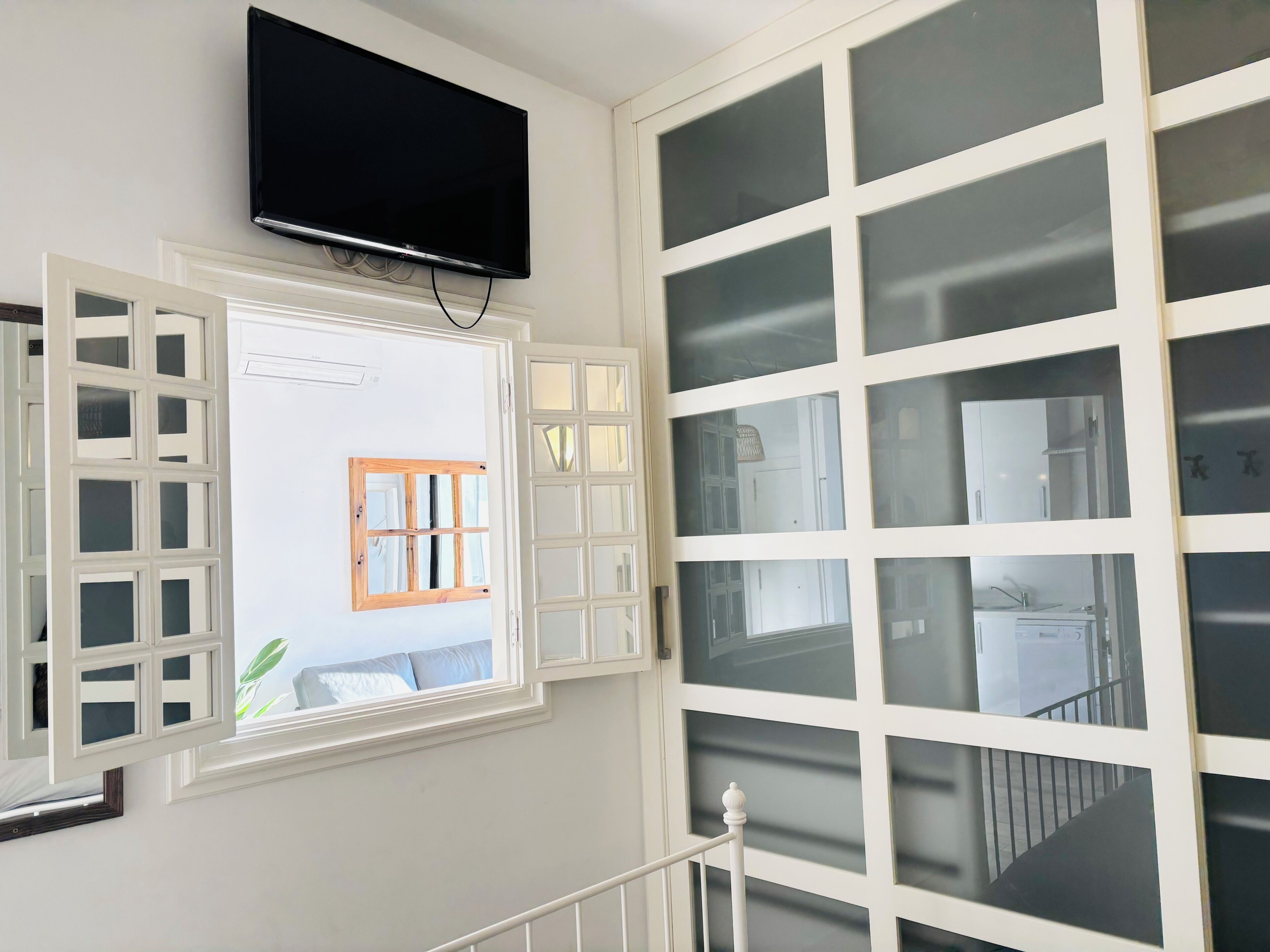 Quarto com uma grande janela, televisão de tela plana acima e corrimão branco em primeiro plano.