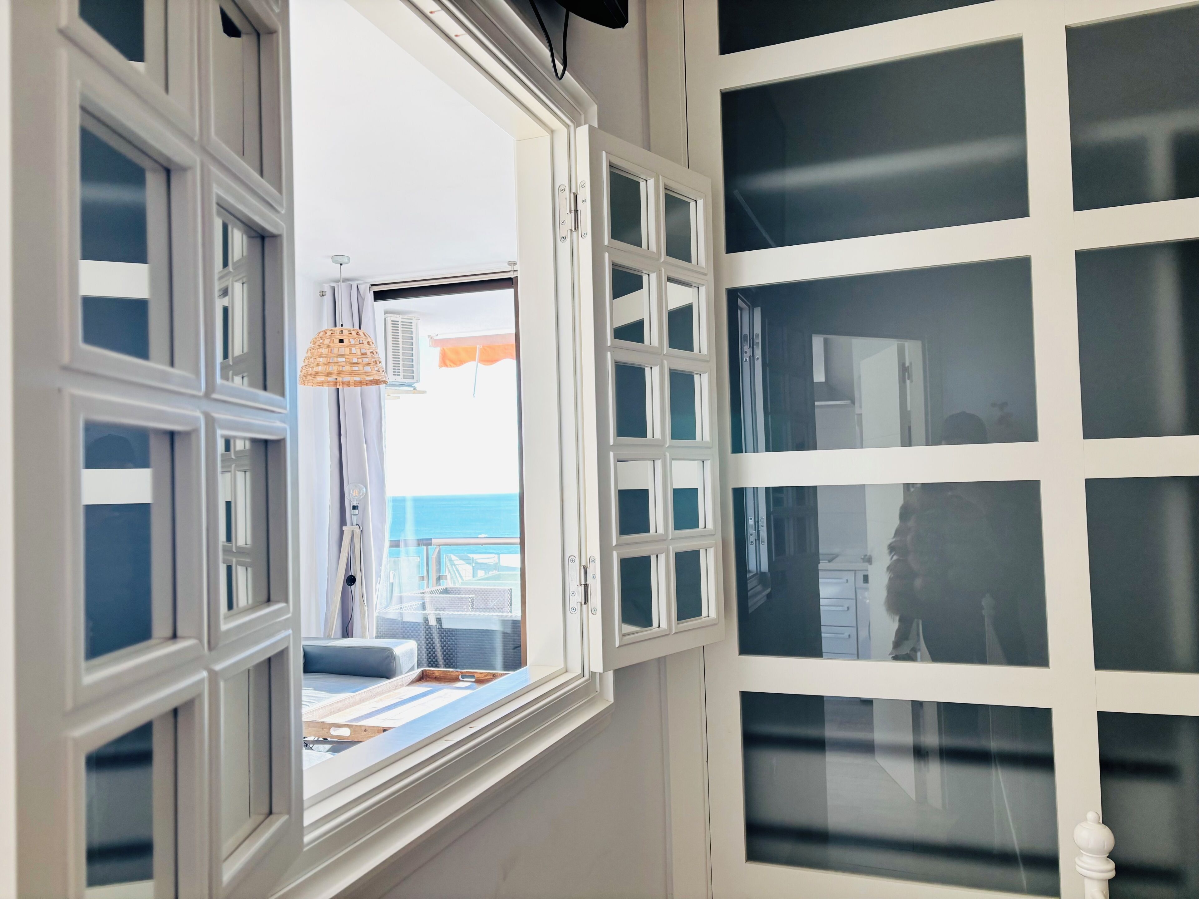 Quarto com uma grande janela, luminária pendente e vista para o mar.