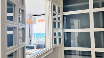 Quarto com uma grande janela, luminária pendente e vista para o mar.