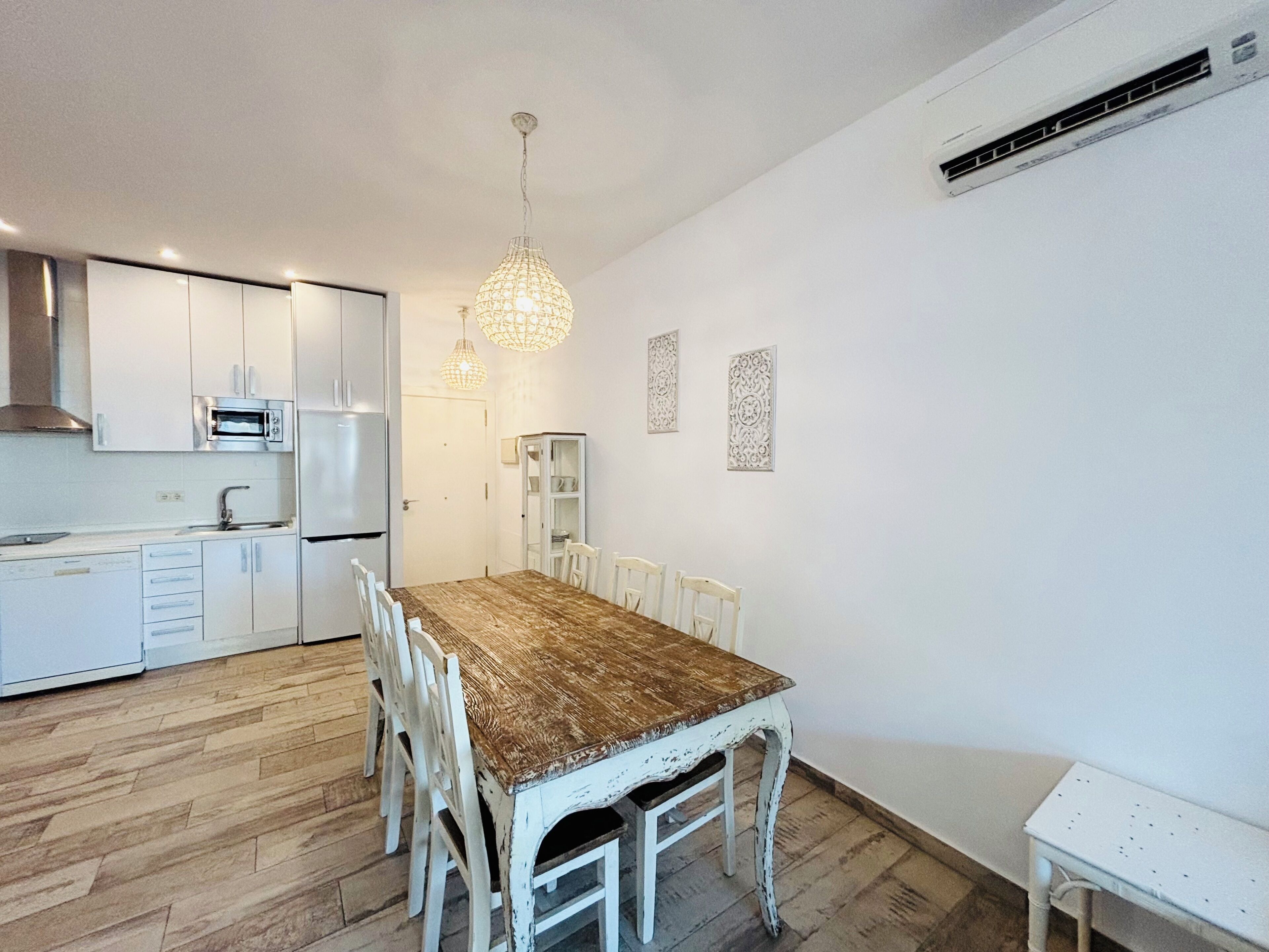 Uma cozinha moderna com armários brancos, uma mesa de jantar de madeira e um lustre.