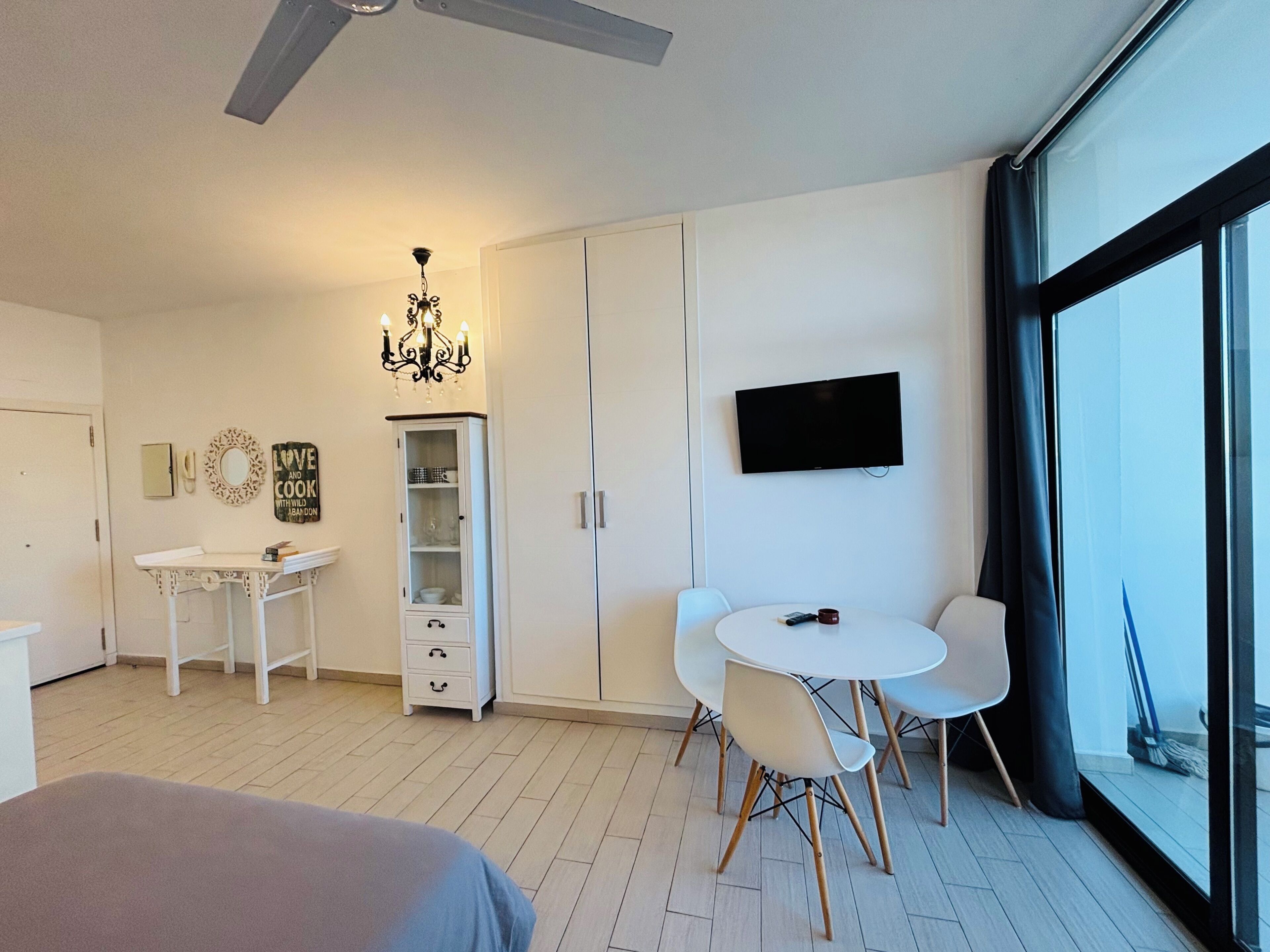 Quarto moderno com mesa de jantar, cadeiras, lustre, televisão e guarda-roupa.