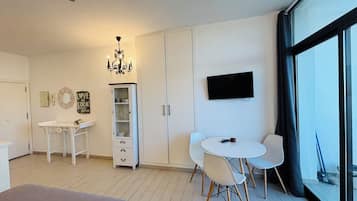 Quarto moderno com mesa de jantar, cadeiras, lustre, televisão e guarda-roupa.