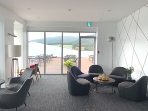 Interior moderno com vista para um lago e montanhas, com área de estar, mesa de centro e cadeiras.