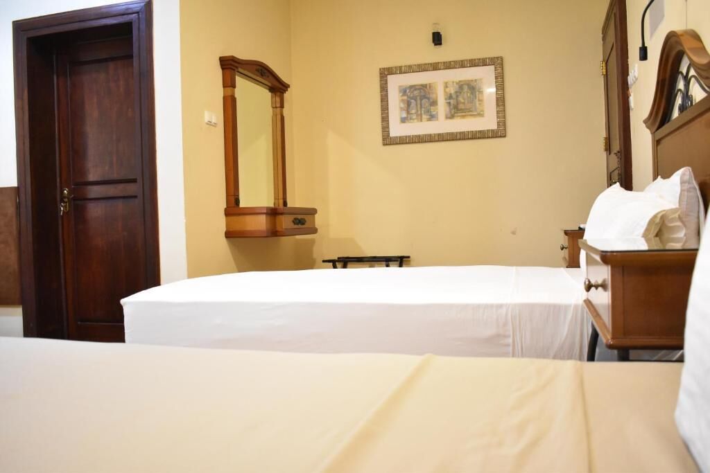 Quarto de hotel com cama, cómoda de madeira, espelho e quadro pendurado na parede.