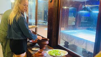 Alguém prepara comida em uma bancada de madeira, perto de uma janela, com uma tigela e um prato com restos de comida.