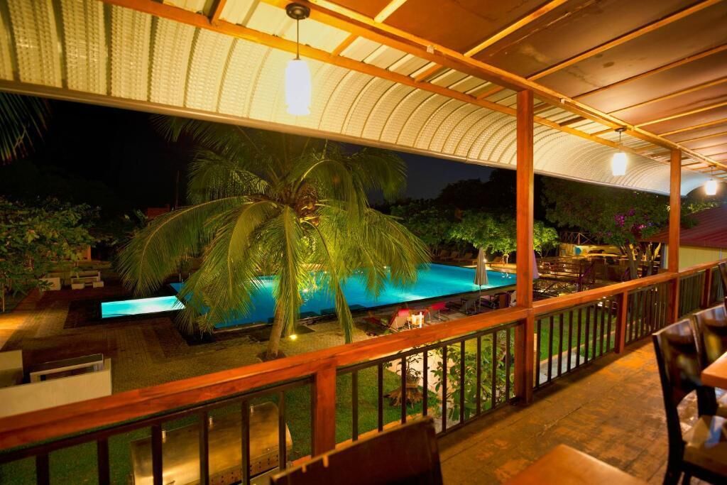 Uma área de piscina ao ar livre com deck de madeira, palmeiras e um espaço de estar coberto.