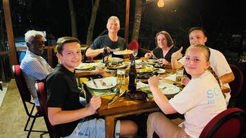 Um grupo de pessoas jantando em uma mesa ao ar livre, com diversos pratos e bebidas.