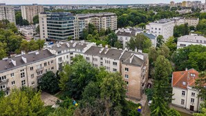 Um edifício alto com vários andares, cercado por áreas verdes e outros edifícios residenciais.