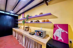 A kitchen with a countertop, shelves with dishes, a microwave, and a painting.