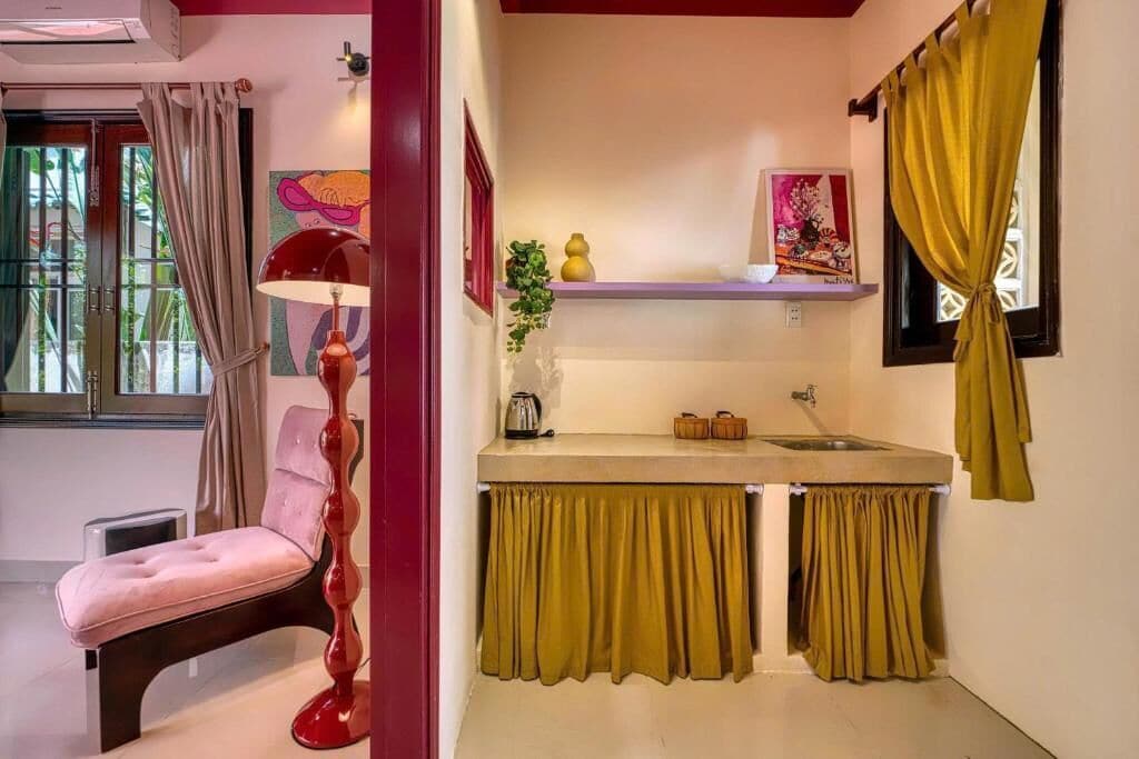 Um espaço compacto com cozinha compacta, uma cadeira, um abajur e uma janela com cortinas.