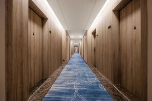 Um longo corredor com portas de madeira, carpete estampado em azul e chão de mármore.