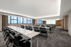 Sala de conferências com várias mesas e cadeiras, amplas janelas com vista para a cidade e uma tela de projeção.