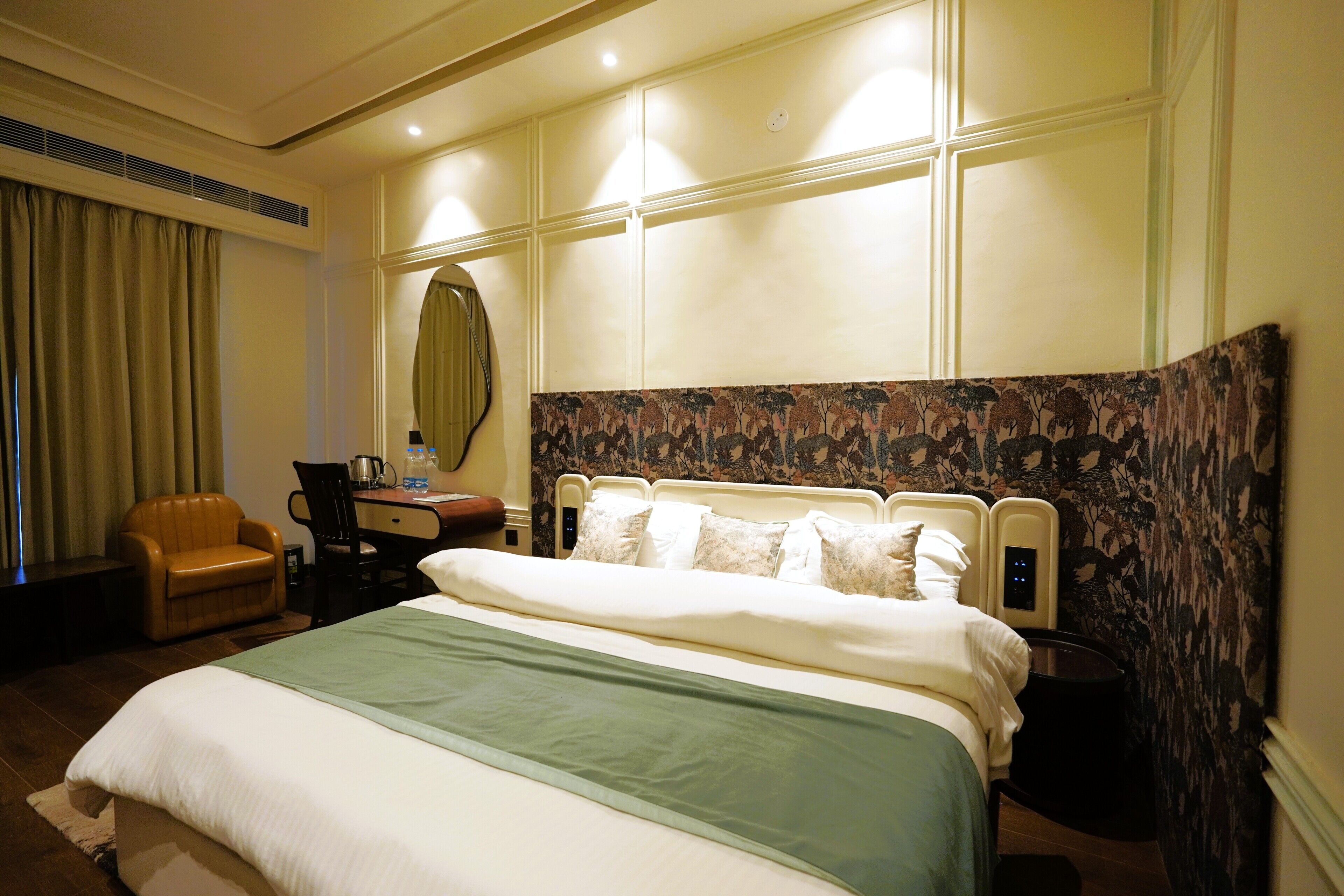 Quarto de hotel com cama, escrivaninha, cadeira e um espelho grande.