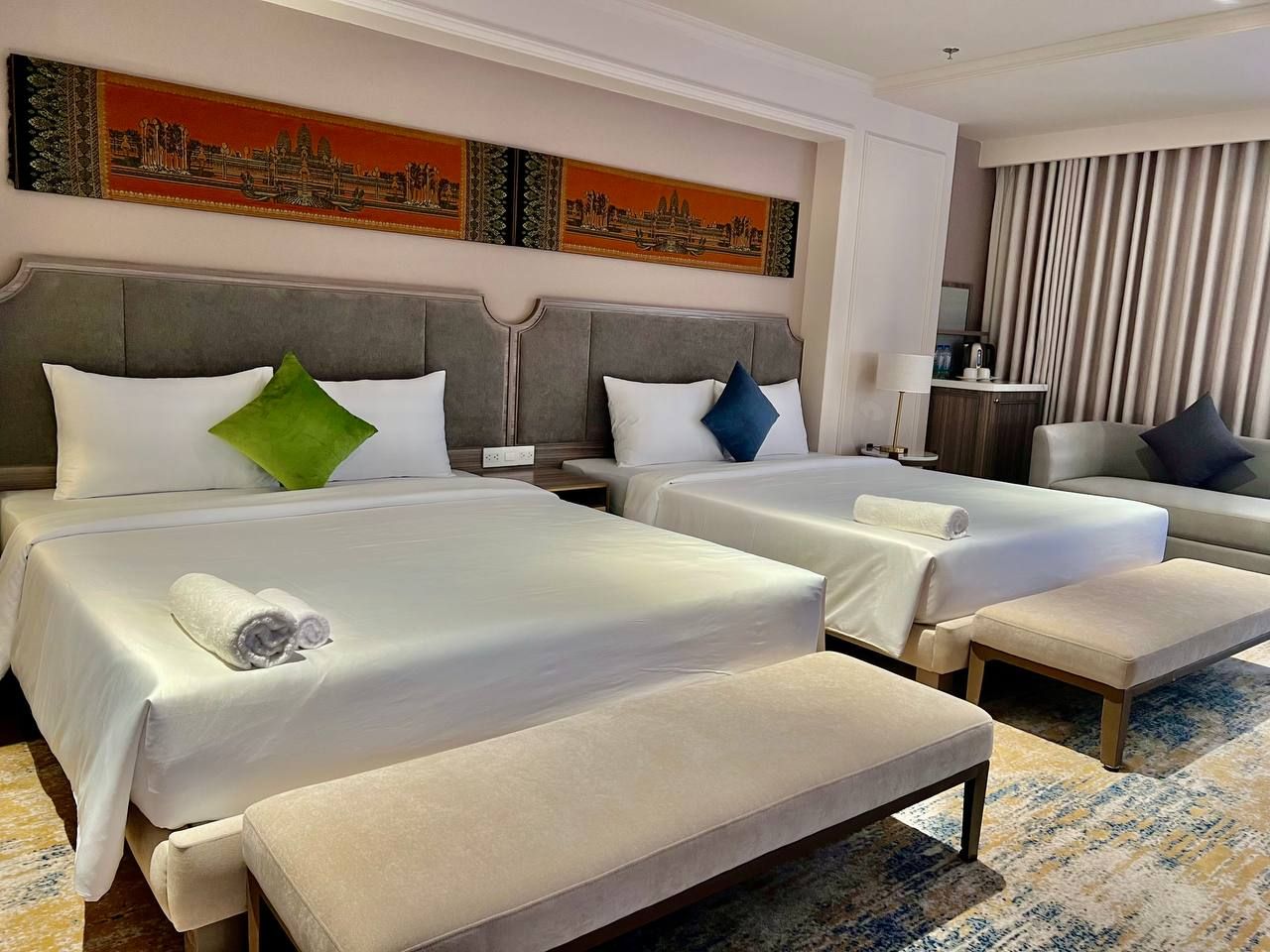 Quarto de hotel com duas camas, um sofá e uma escrivaninha.