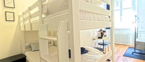 Quarto com beliche, escrivaninha, cadeira, radiador e janela.