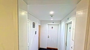 Um corredor estreito com chão de madeira escura, paredes brancas e portas numeradas 34 e 35.