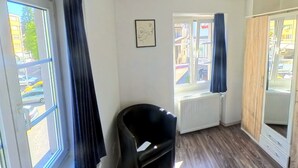 Quarto com cadeira preta, radiador e janela com cortinas.