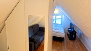 Quarto sótão pequeno e triangular com cama, sofá e televisão.