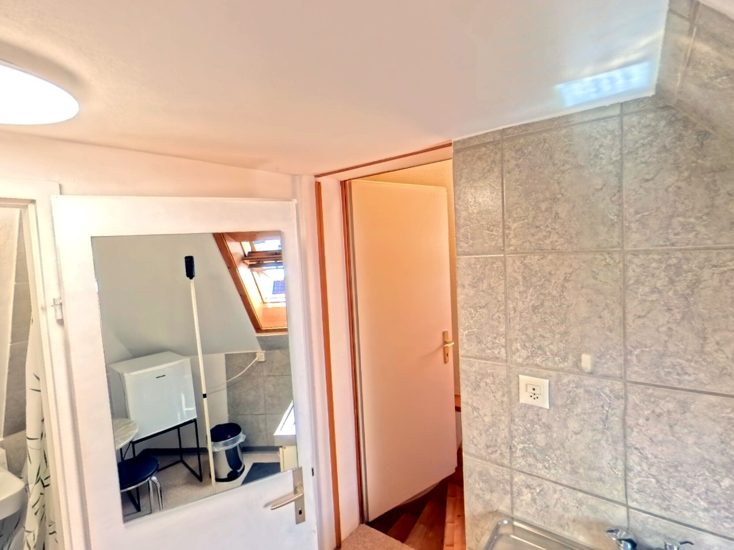 Casa de banho com chuveiro, sanita e lavatório. Uma porta dá para outro espaço.