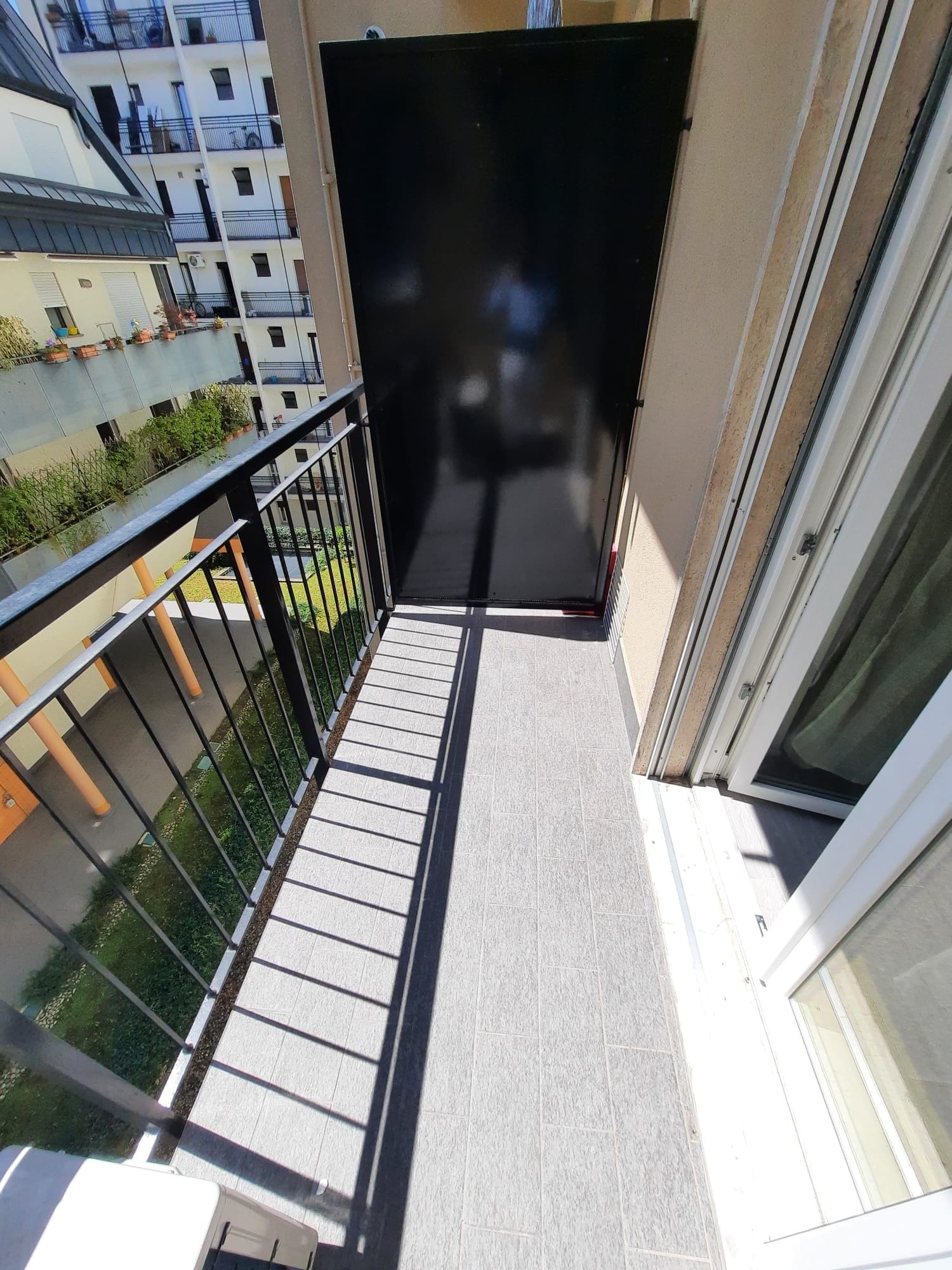 Uma varanda com grades de metal, uma porta e vista para edifícios vizinhos.