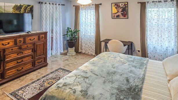 Quarto com cama, cômoda, televisão, cortinas e um quadro.