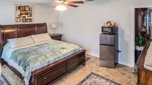 Quarto com cama, mesas de cabeceira, ventilador de teto, geladeira e uma decoração na parede.