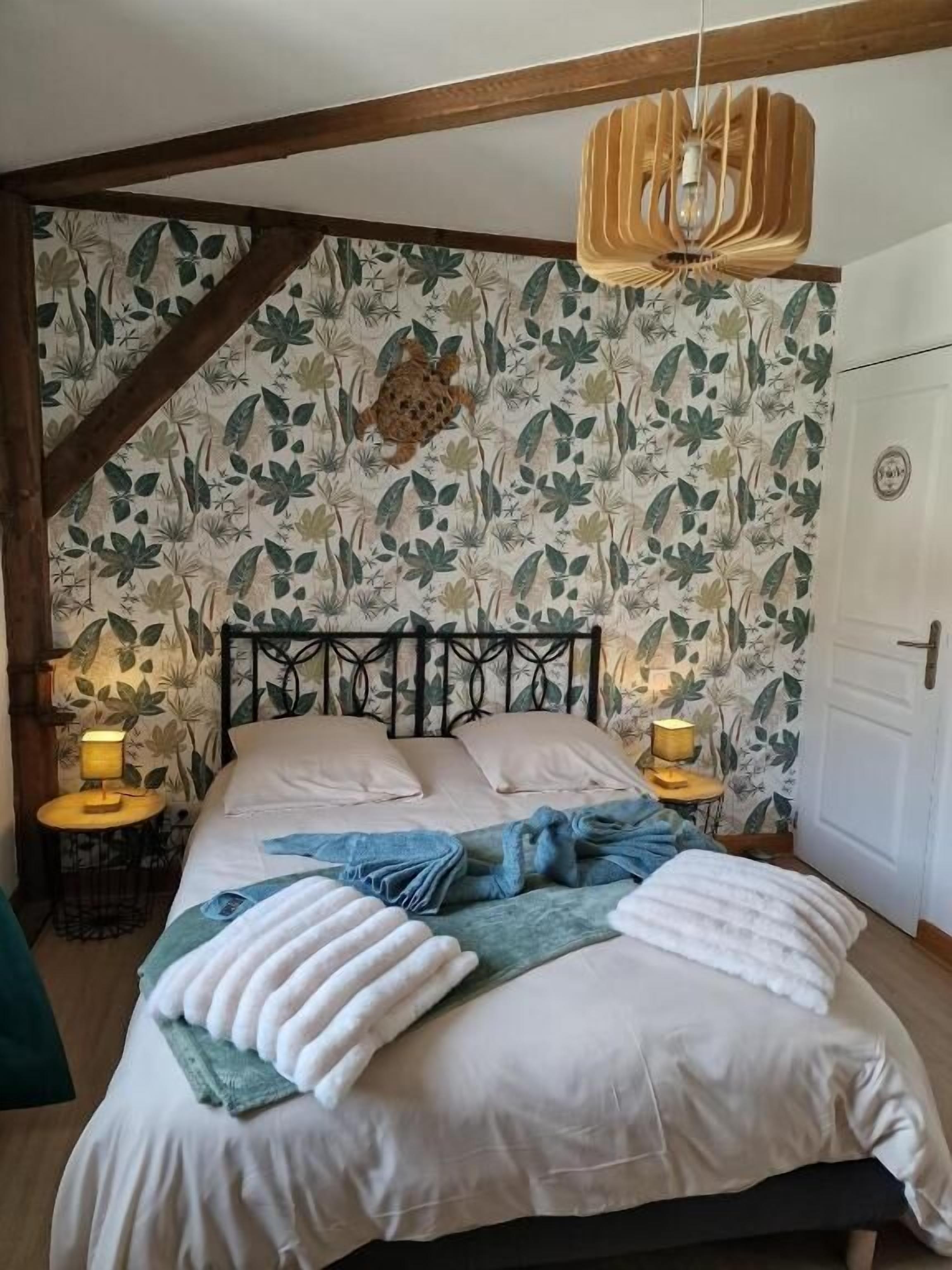 Quarto com cama, vigas de madeira, papel de parede floral e luminária pendente.
