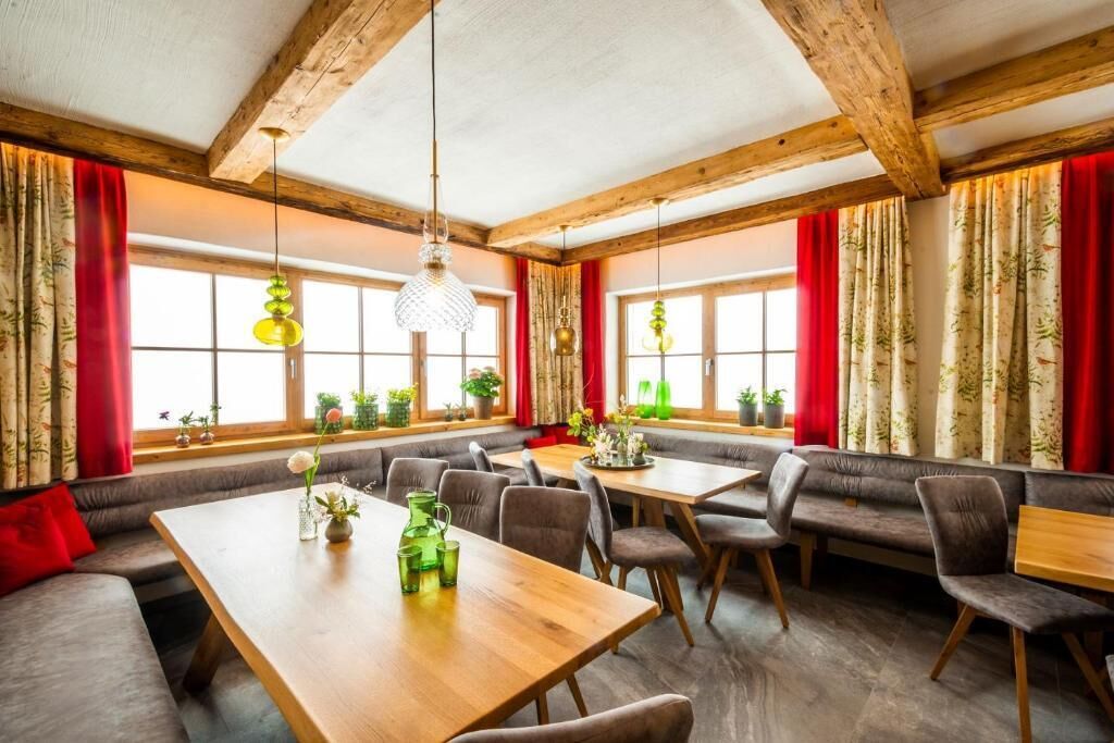 Restaurante com vigas de madeira, janelas amplas com cortinas vermelhas e diversos tipos de assentos, incluindo mesas e bancos.