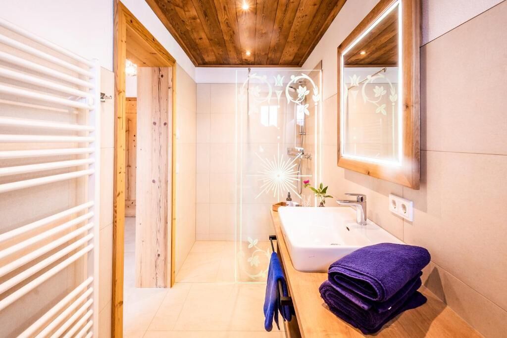 Uma casa de banho moderna com teto de madeira, cabine de duche em vidro, lavatório branco e espelho.