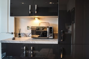 Uma cozinha com micro-ondas embutido, cafeteira e uma pequena mesa com um controle remoto e um objeto decorativo.