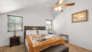 Quarto com cama, um banquinho, duas mesas de cabeceira, ventilador de teto e um quadro na parede.