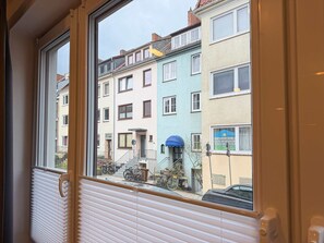 Janela com vista para um prédio residencial de vários andares com varandas e uma bicicleta estacionada na frente.