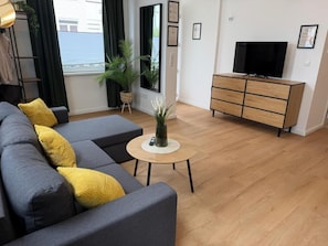 Uma sala de estar moderna com um sofá cinzento, mesa de centro de madeira e um móvel para televisão.