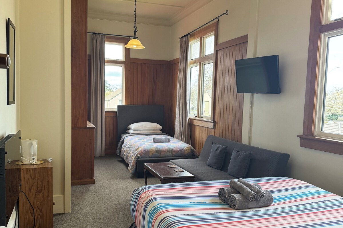 Quarto de hotel com uma cama grande, um sofá, uma escrivaninha e uma televisão.