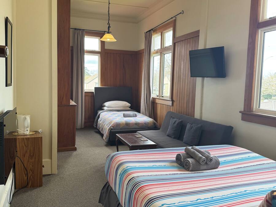 Quarto de hotel com uma cama grande, um sofá, uma escrivaninha e uma televisão.