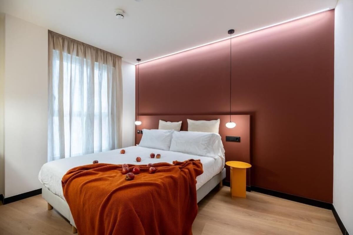 Quarto moderno com cama, mesa de cabeceira e janela com cortinas.