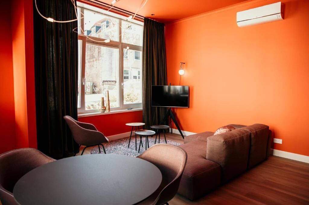 Uma sala de estar moderna com uma janela grande, uma TV de tela plana, um sofá e uma mesa redonda.