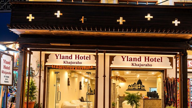 Exterior do Hotel Yland Khajuraho, com placa, entrada e plantas em vasos.