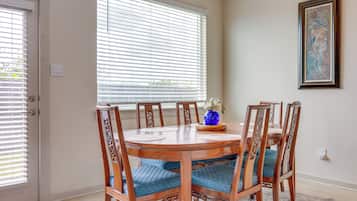 Uma sala de jantar com uma mesa de madeira, seis cadeiras e um vaso com flores.