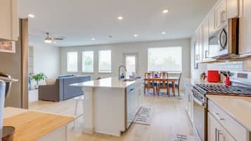 Uma cozinha moderna com uma ilha central, uma sala de jantar com mesa e cadeiras, e uma sala de estar com sofá.