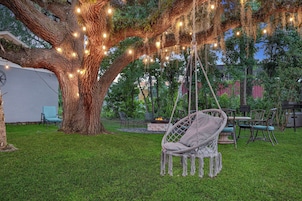 Uma árvore com luzes penduradas, uma cadeira de balanço e uma lareira em um quintal gramado.