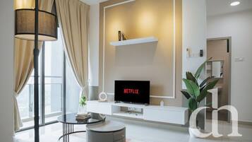 Uma sala de estar moderna com televisão de tela plana, uma mesa de centro redonda e uma janela grande com cortinas.