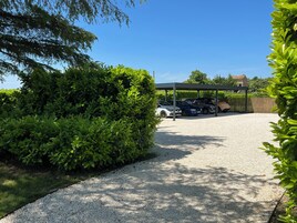 Uma estrada de cascalho leva a uma área de estacionamento coberta, com carros estacionados sob uma proteção.