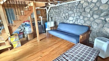 Interior acolhedor de uma cabana com escada de madeira, parede de pedra, sofá azul e colcha xadrez.