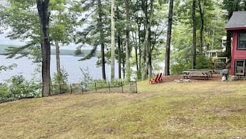 Um terreno à beira do lago com um edifício vermelho, área de piquenique e árvores altas.