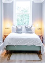 Quarto com cama, duas luminárias de cabeceira, uma janela e vista para árvores.